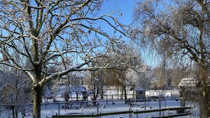 Um parque coberto de neve, com área cercada, bancos e céu claro.