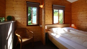 Quarto de cabana de madeira com cama, cadeira e duas janelas.
