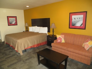 Quarto de hotel com cama, sofá, mesa de cabeceira, duas luminárias e duas imagens emolduradas nas paredes.