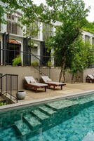 Piscina com degraus de acesso, rodeada por espreguiçadeiras e uma escadaria que leva a um edifício.