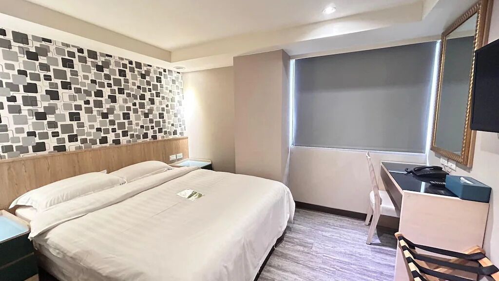 Quarto de hotel com uma cama grande, uma escrivaninha, uma cadeira, um espelho e uma parede com padrão em mosaico.