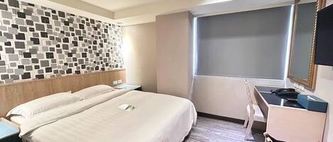 Quarto de hotel com uma cama grande, uma escrivaninha, uma cadeira, um espelho e uma parede com padrão em mosaico.