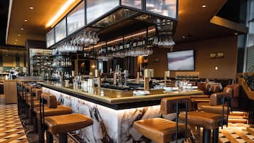 Uma área de bar com bancada de mármore, vários bancos e uma variedade de garrafas e copos.