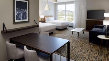 Quarto de hotel com cama, escrivaninha, cadeira, televisão e janela com vista.