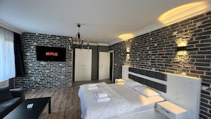 Quarto de hotel moderno com parede de tijolos, televisão de tela plana, cama grande, mesas de cabeceira e sofá.