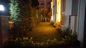 Área de jardim bem iluminada com um caminho que leva à entrada de um edifício.