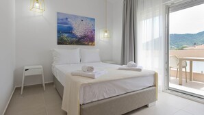 Quarto de hotel com cama, mesa de cabeceira, um quadro e vista para o exterior.