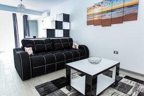 Uma sala de estar moderna com um sofá preto, uma mesa de centro branca e uma grande pintura de um pôr do sol.