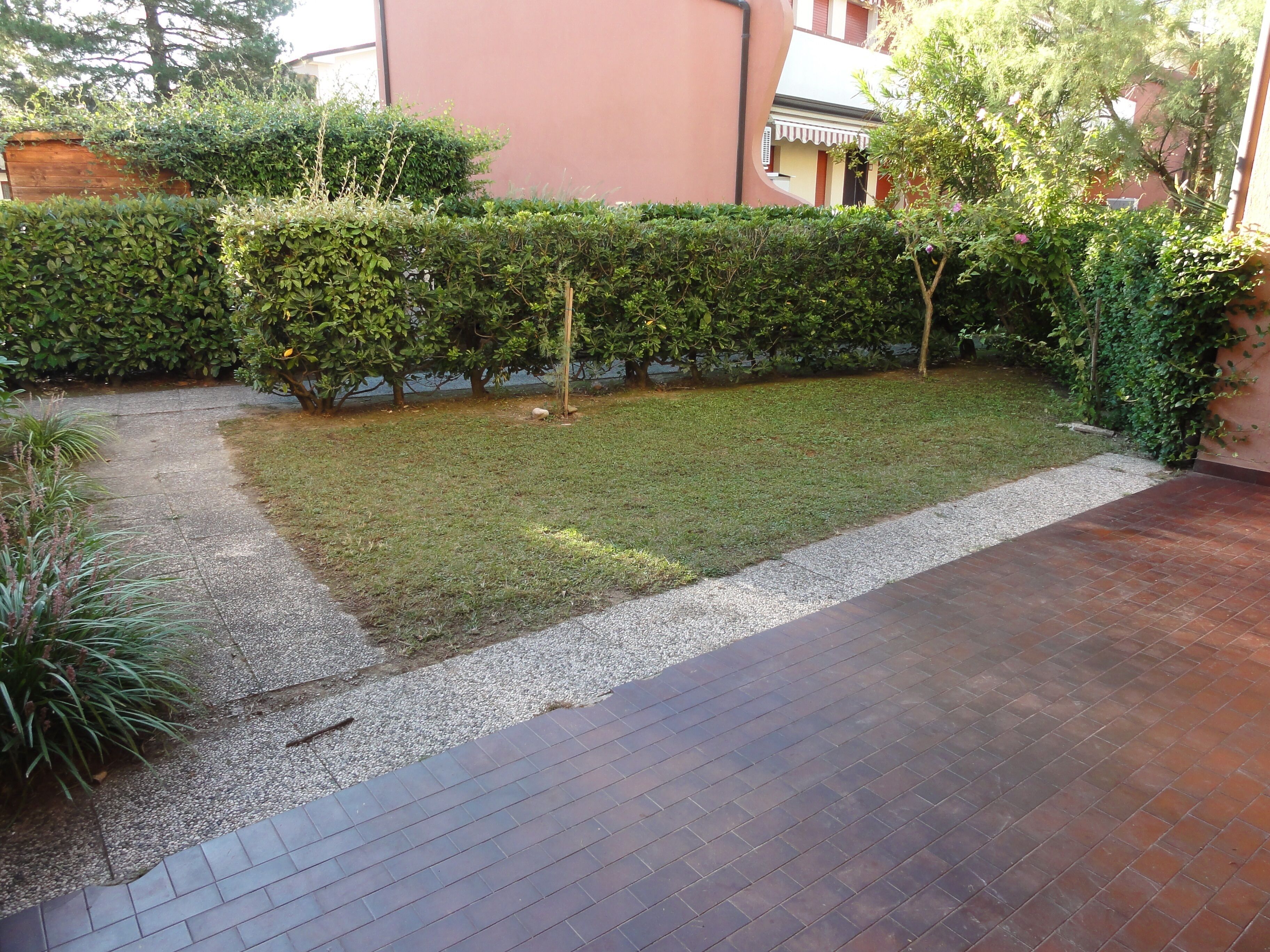 Um jardim bem cuidado com um caminho pavimentado, sebes bem aparadas e um gramado.