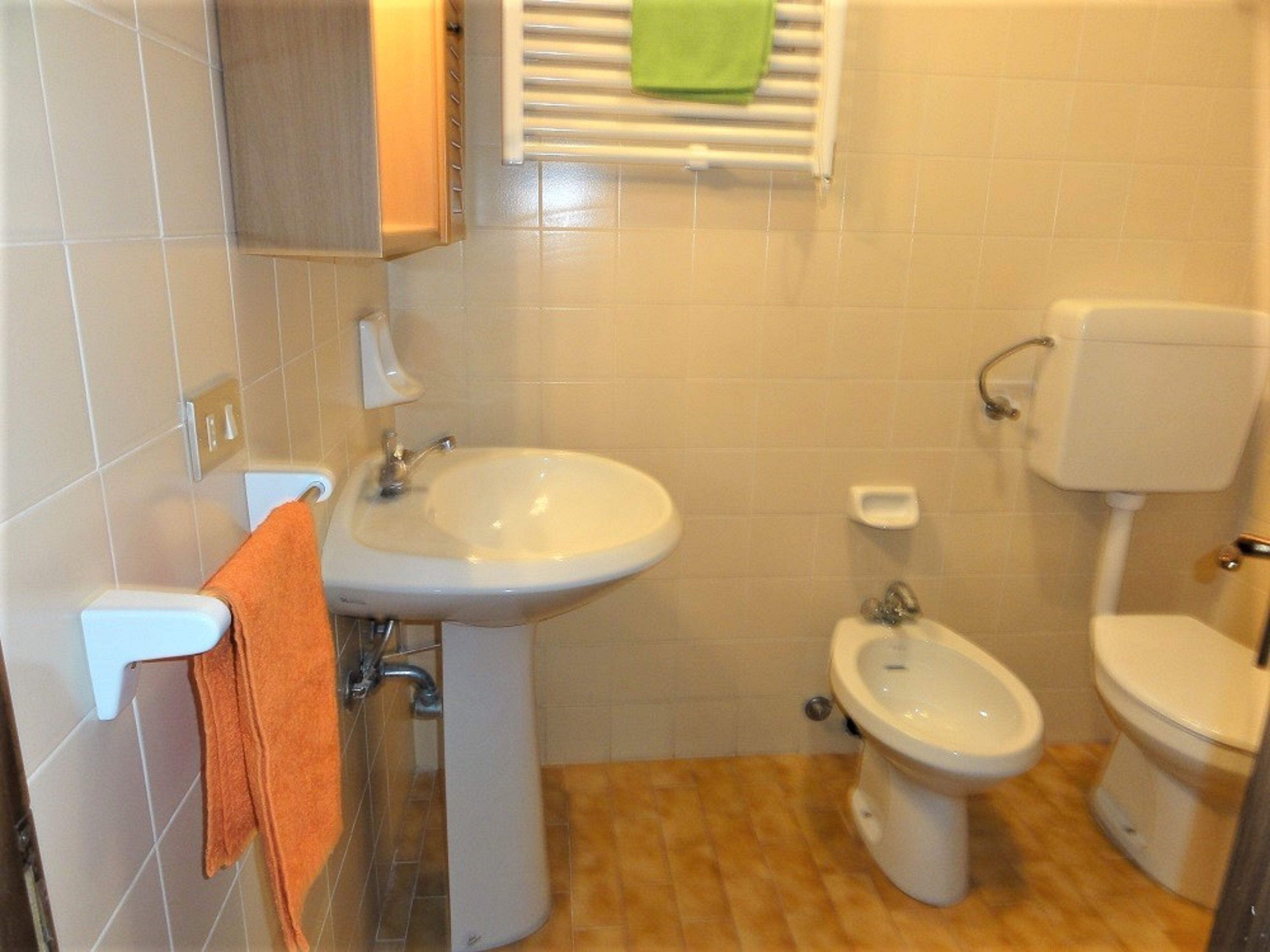 Casa de banho com lavatório, sanita, bidé e um porta-toalhas com toalha.