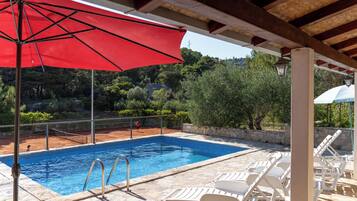 Uma piscina com guarda-sol vermelho, cadeiras de descanso brancas e um deck de pedra.