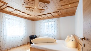 Quarto moderno com teto de madeira, cama com encosto e cortinas leves.