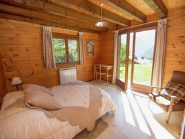 Quarto de cabana de madeira com uma cama, uma mesa, uma cadeira e vista para o exterior.