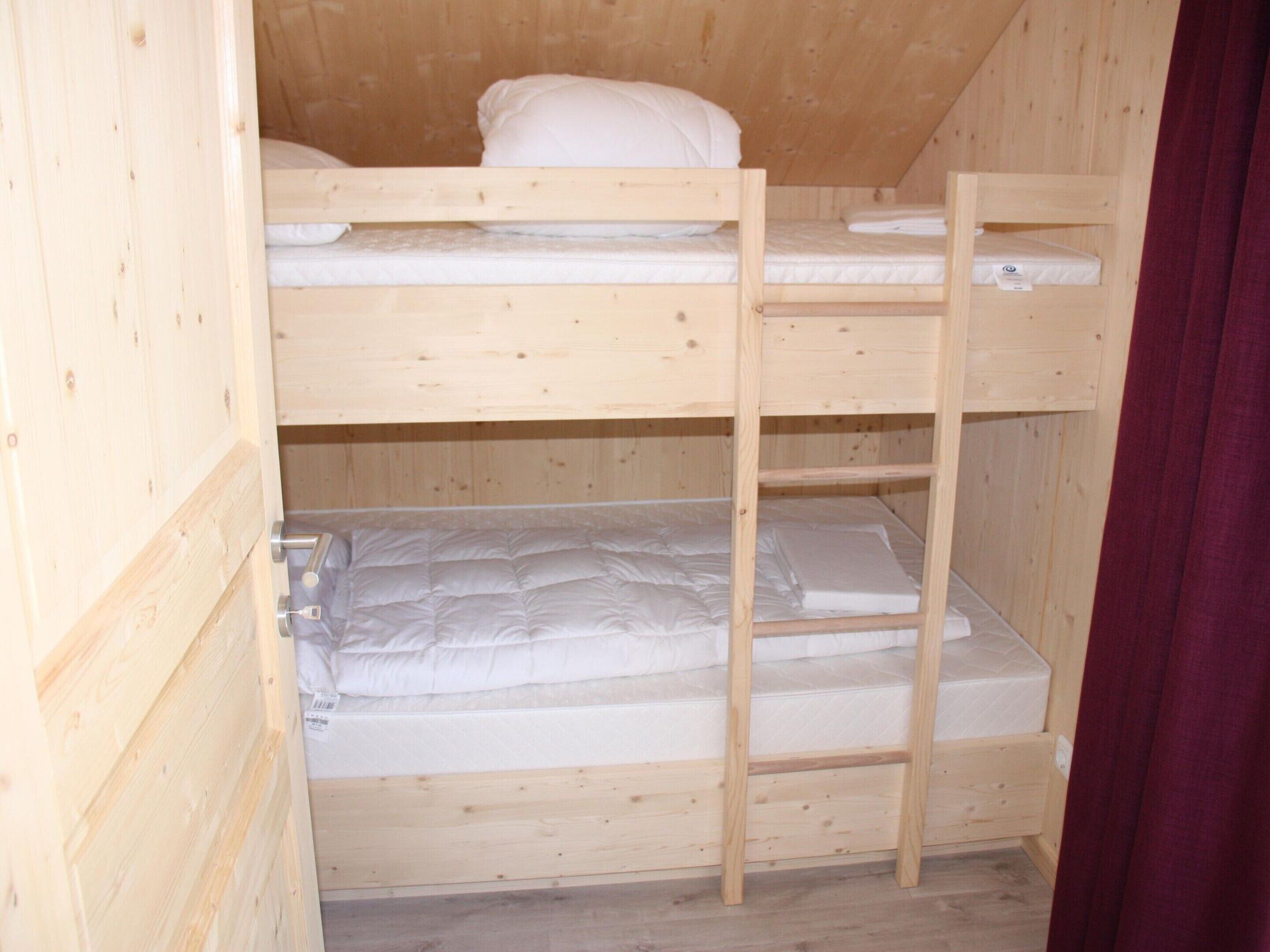 Uma cama beliche de madeira com escada, colchão e travesseiro.