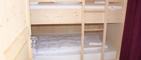 Uma cama beliche de madeira com escada, colchão e travesseiro.