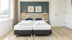 Uma cama de casal com duas mesas de cabeceira, uma janela com cortinas e uma porta.