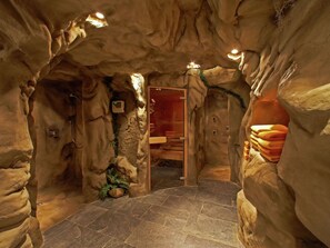 Interior que lembra uma gruta, com porta de madeira, paredes de pedra e chão de azulejos.