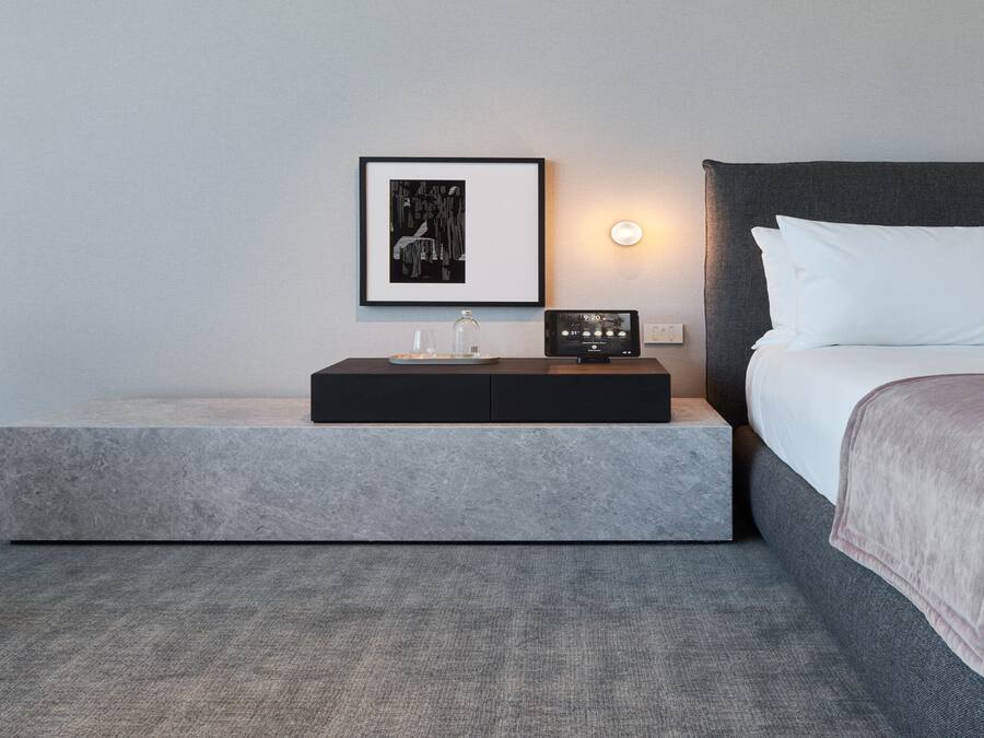 Quarto moderno com cama, mesa de cabeceira e relógio fixado na parede.