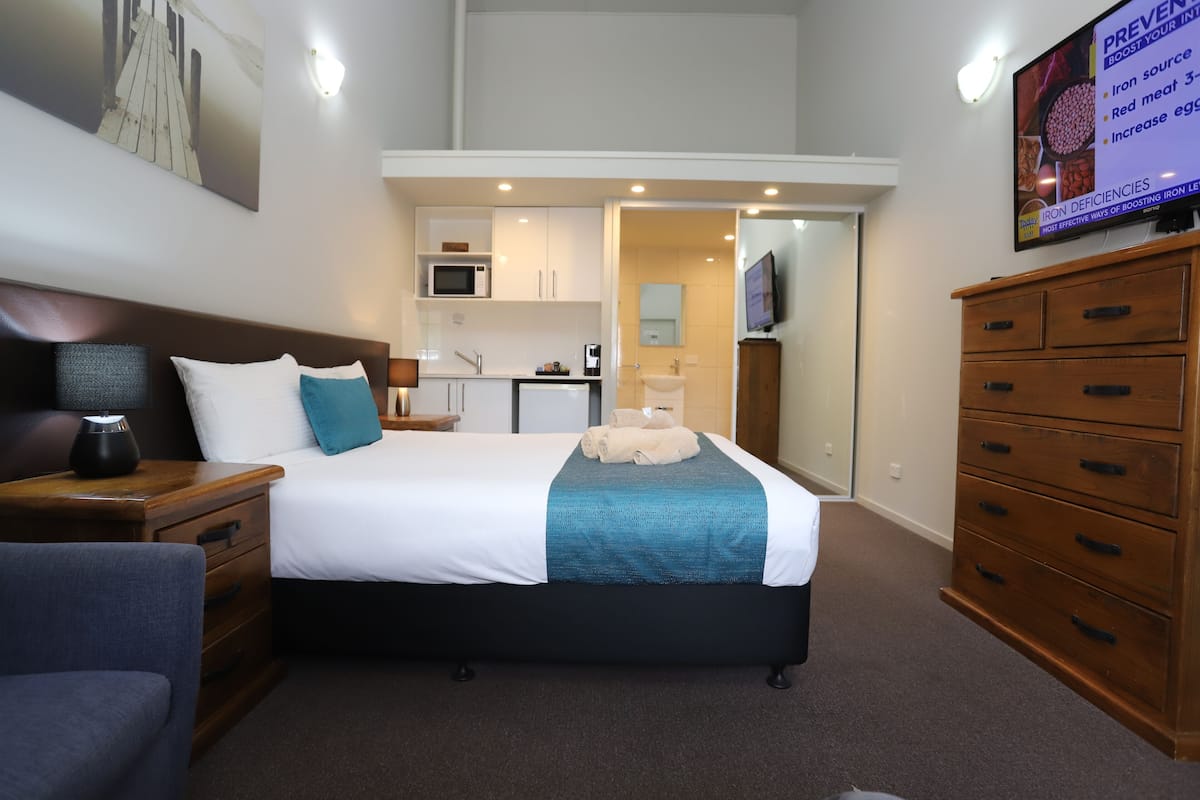 Quarto de hotel com cama, mesa de cabeceira, abajur e televisão na parede.