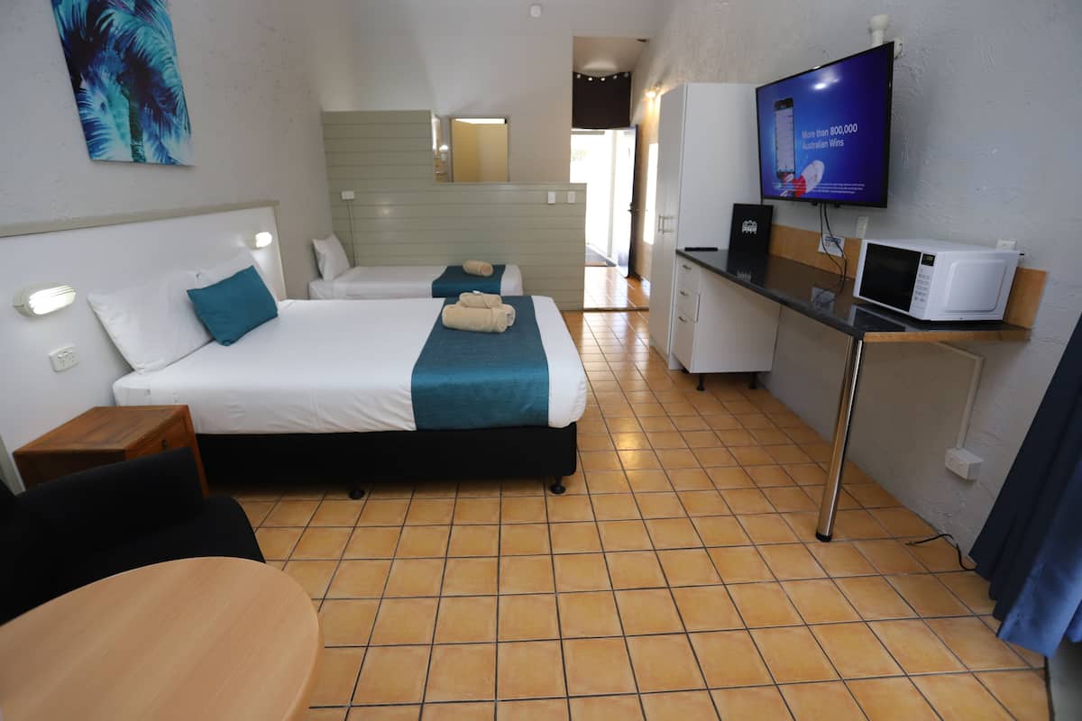 Quarto de hotel com duas camas, televisão, micro-ondas e uma pequena mesa.