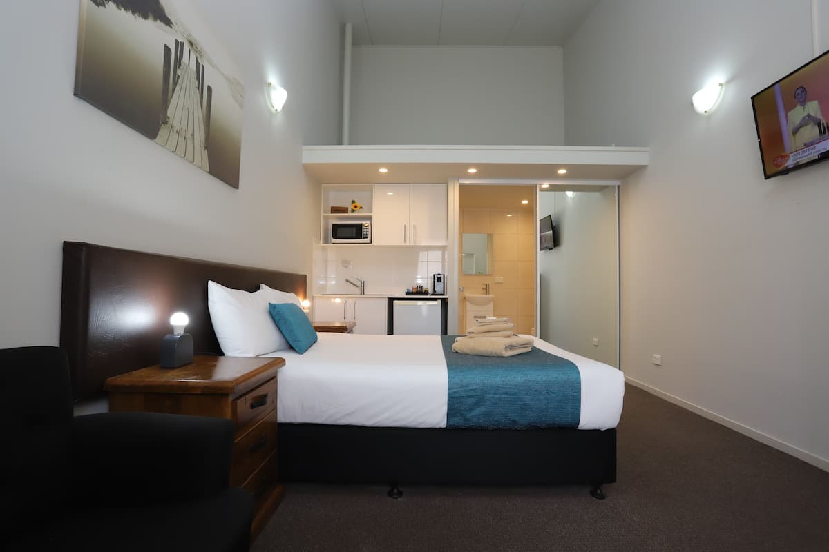 Quarto de hotel moderno com cama, mesa de cabeceira e pequena área de trabalho.