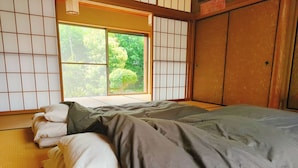 Um quarto em estilo japonês tradicional, com tatame, futon, portas deslizantes shoji e vista para o verde lá fora.