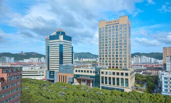 Um hotel moderno com fachada de vidro marcante, rodeado por outros edifícios e vegetação.