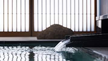 Uma fonte com um riacho que deságua numa piscina espelhada, com venezianas verticais ao fundo.