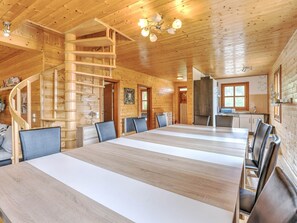 Interior de uma cabana de madeira, com área de jantar, cozinha e escada em espiral.