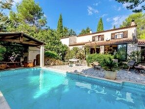 Uma área de piscina com espreguiçadeiras, um espaço de estar coberto e um edifício com telhado telhado.