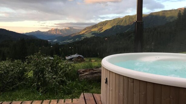 Uma banheira de hidromassagem numa varanda de madeira, com uma paisagem montanhosa ao fundo.