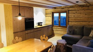 Interior acolhedor de uma cabana com uma mesa de jantar de madeira, um sofá e uma área de cozinha com janela.