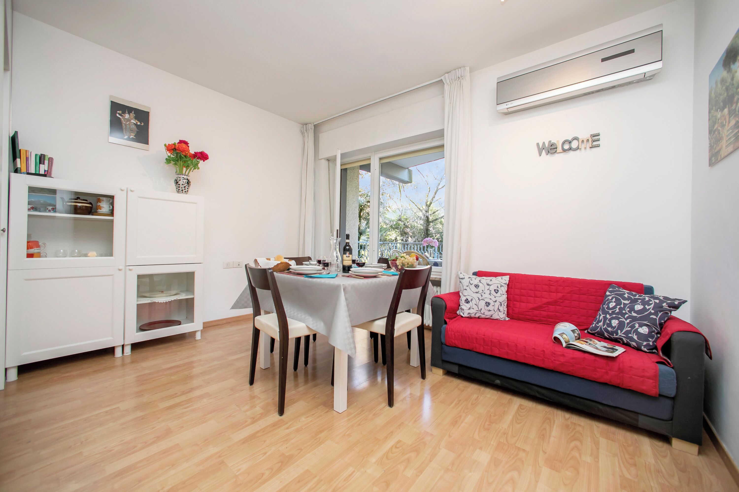 Uma sala de estar moderna com uma mesa de jantar, um sofá vermelho e um letreiro com a palavra 'Welcome' na parede.