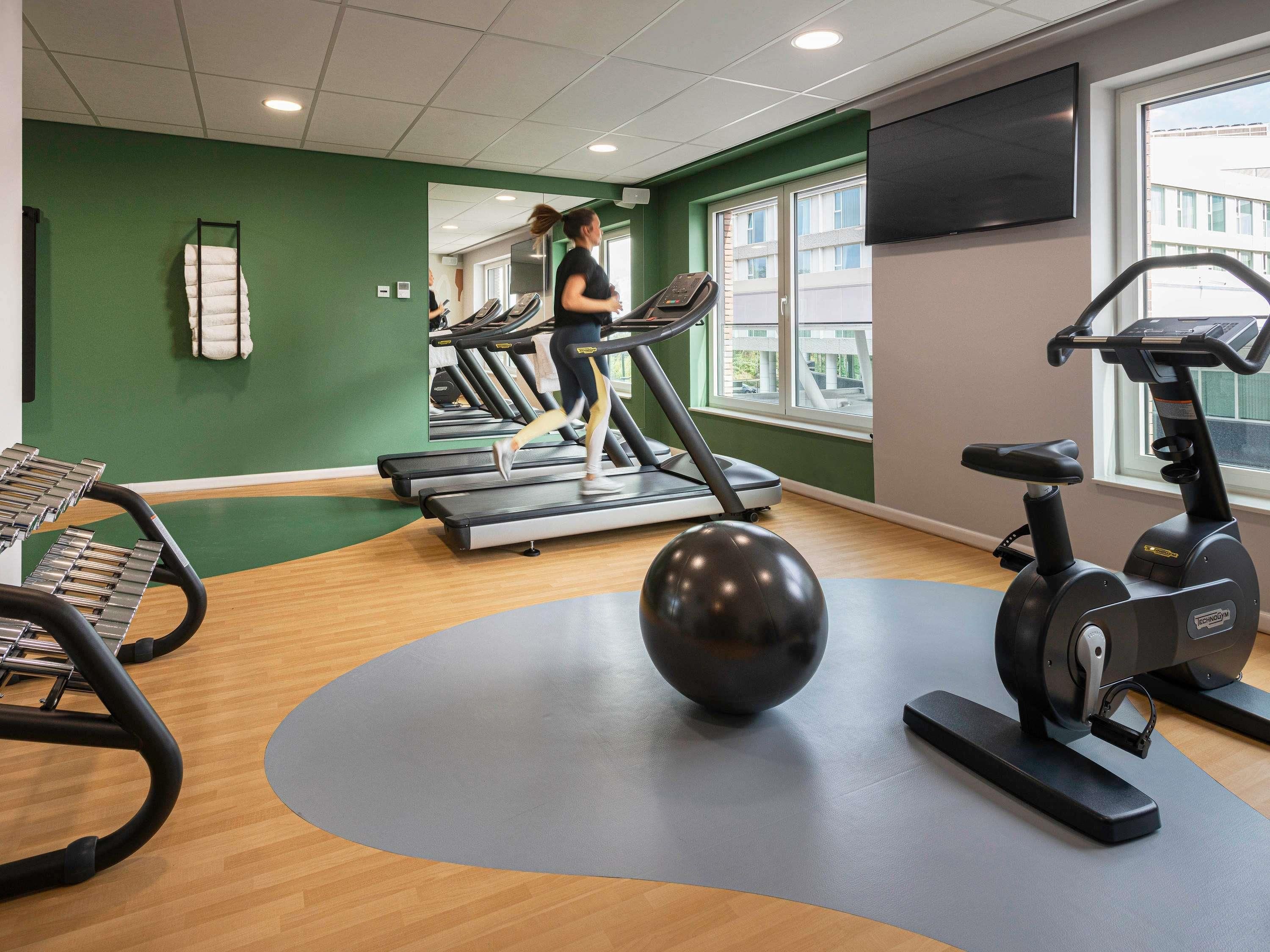 Academia com esteiras, elíptico e uma bola de exercícios grande.