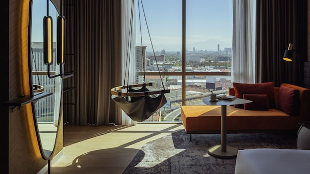 Quarto de hotel moderno com uma janela grande, uma cadeira suspensa, um sofá e uma mesa redonda.