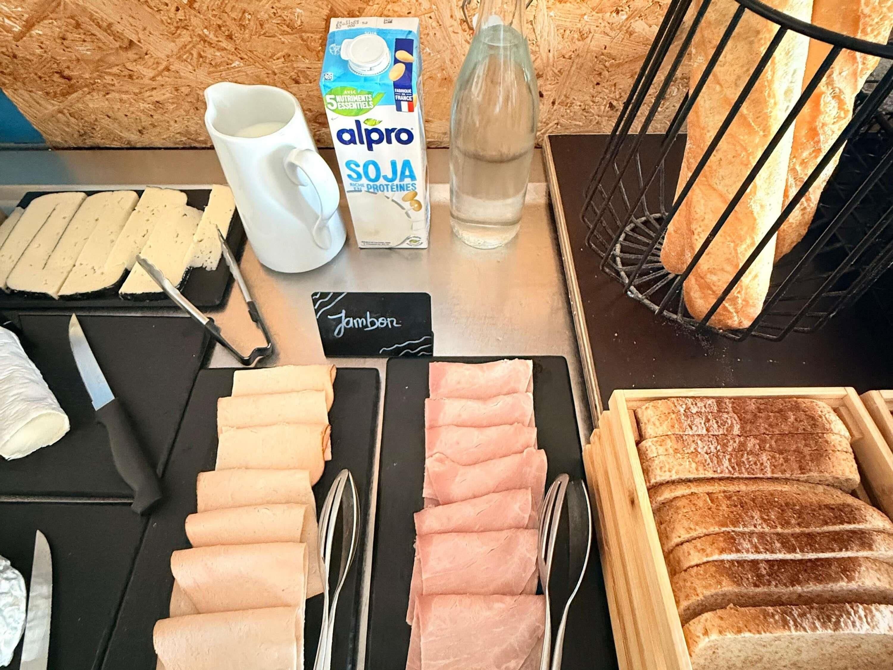 Buffet de café da manhã com diversos alimentos, incluindo pão, doces e um pacote de leite.