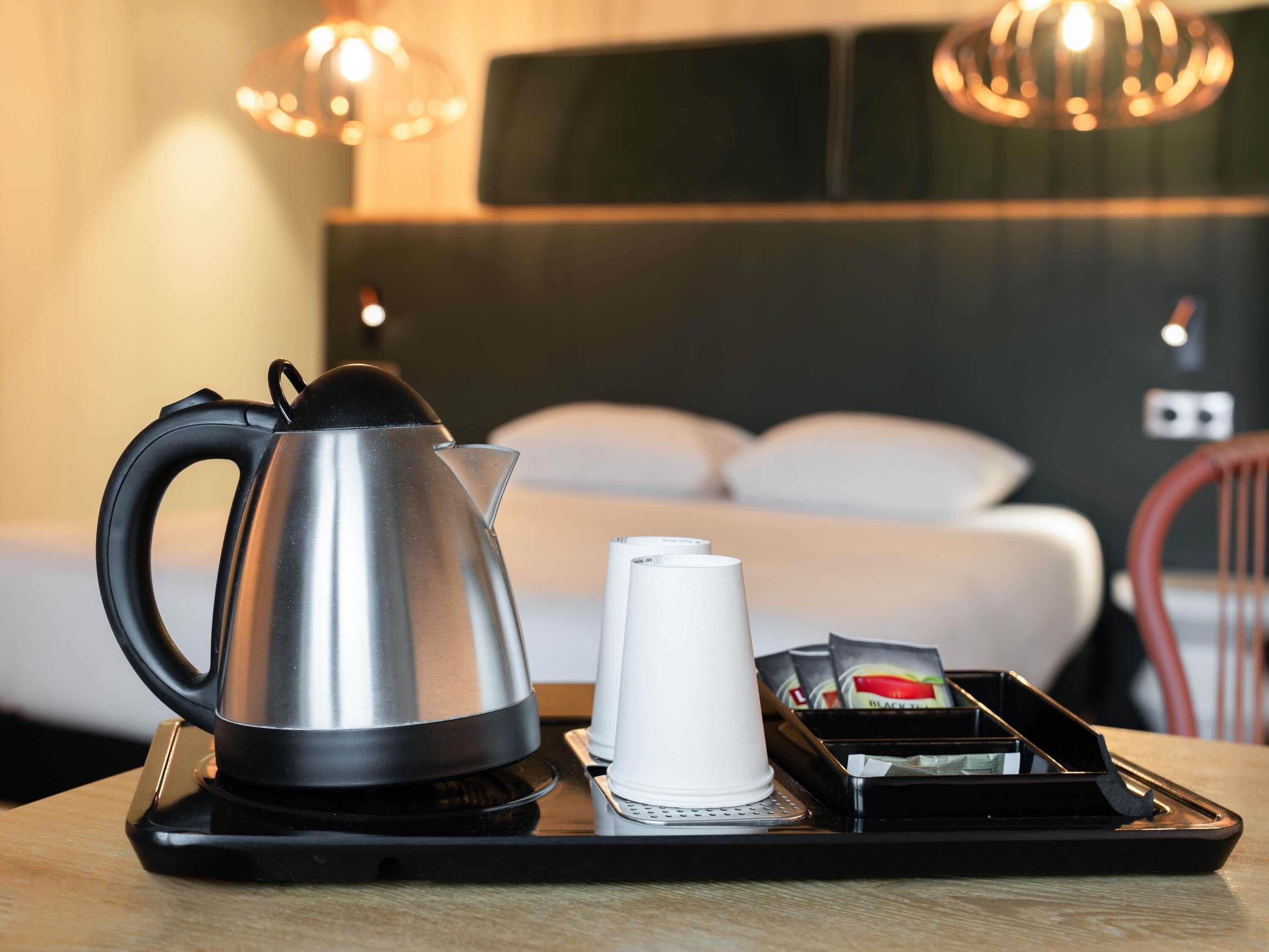 Quarto de hotel com uma cama, mesa de cabeceira com chaleira, chávenas e um tabuleiro com saquinhos de chá.