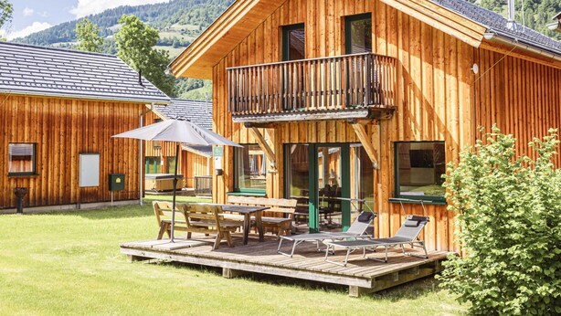 Uma cabana de madeira com varanda, mobiliário externo e vista para a paisagem ao redor.