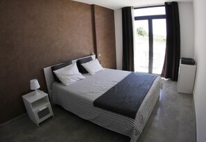 Quarto de hotel moderno com uma cama grande, uma mesa de cabeceira e vista para o exterior.