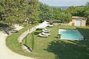 Uma área de piscina com muro de pedra, espreguiçadeiras e um pequeno edifício com porta.
