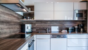 Uma cozinha moderna com armários brancos, forno embutido, micro-ondas e máquina de café.