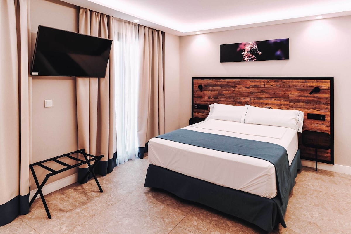 Quarto de hotel moderno com uma cama grande, televisão de tela plana na parede e cabeceira de madeira.