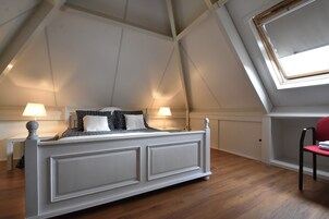 Quarto com teto inclinado, cama com cabeceira branca, duas luminárias de cabeceira e um claraboia.