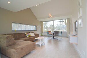 Uma sala de estar moderna com um sofá de couro marrom, uma mesa de centro branca e uma área de jantar com mesa e cadeiras.