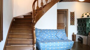 Escada de madeira que leva a uma porta, um sofá azul com padrão e um armário verde com objetos decorativos.