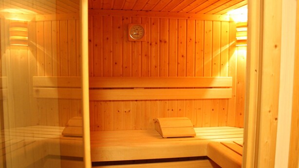 Uma sauna de madeira com bancos e termômetro visível.