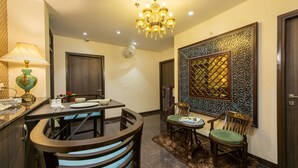 Uma sala de jantar com candelabro, uma mesa com cadeiras, um painel decorativo e uma porta.