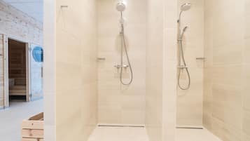 Um banheiro moderno com duas chuveiras, piso de madeira e área de sauna visível.