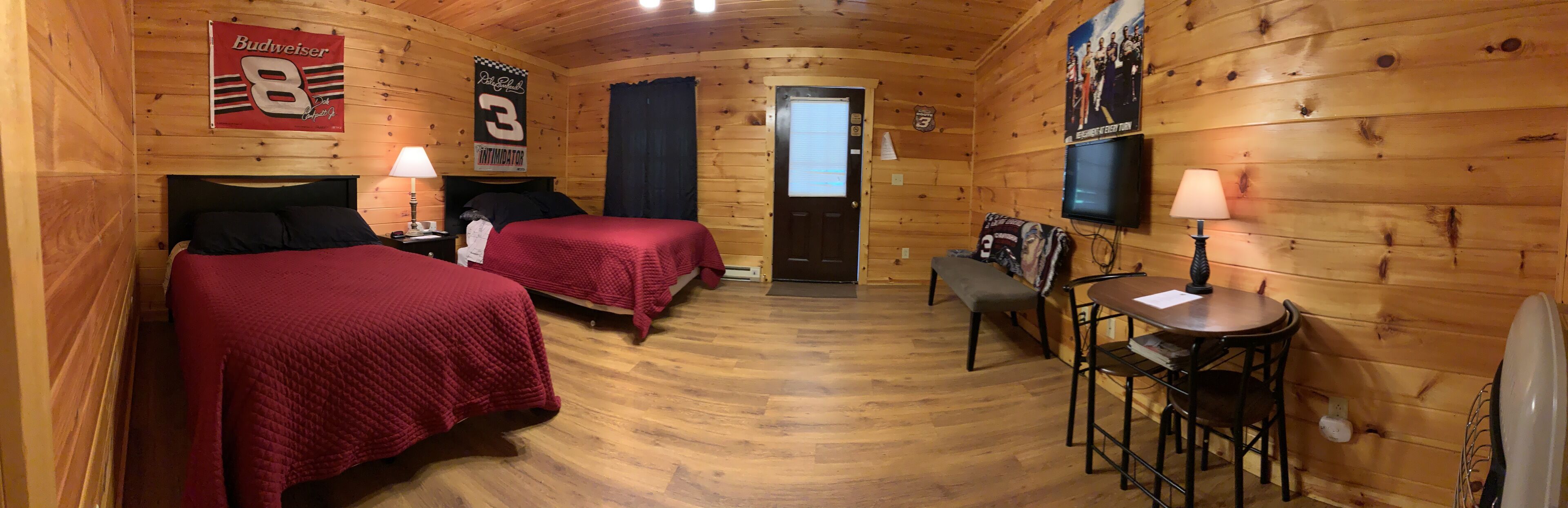 Quarto de cabana de madeira com duas camas, uma televisão, uma mesa e um banco.