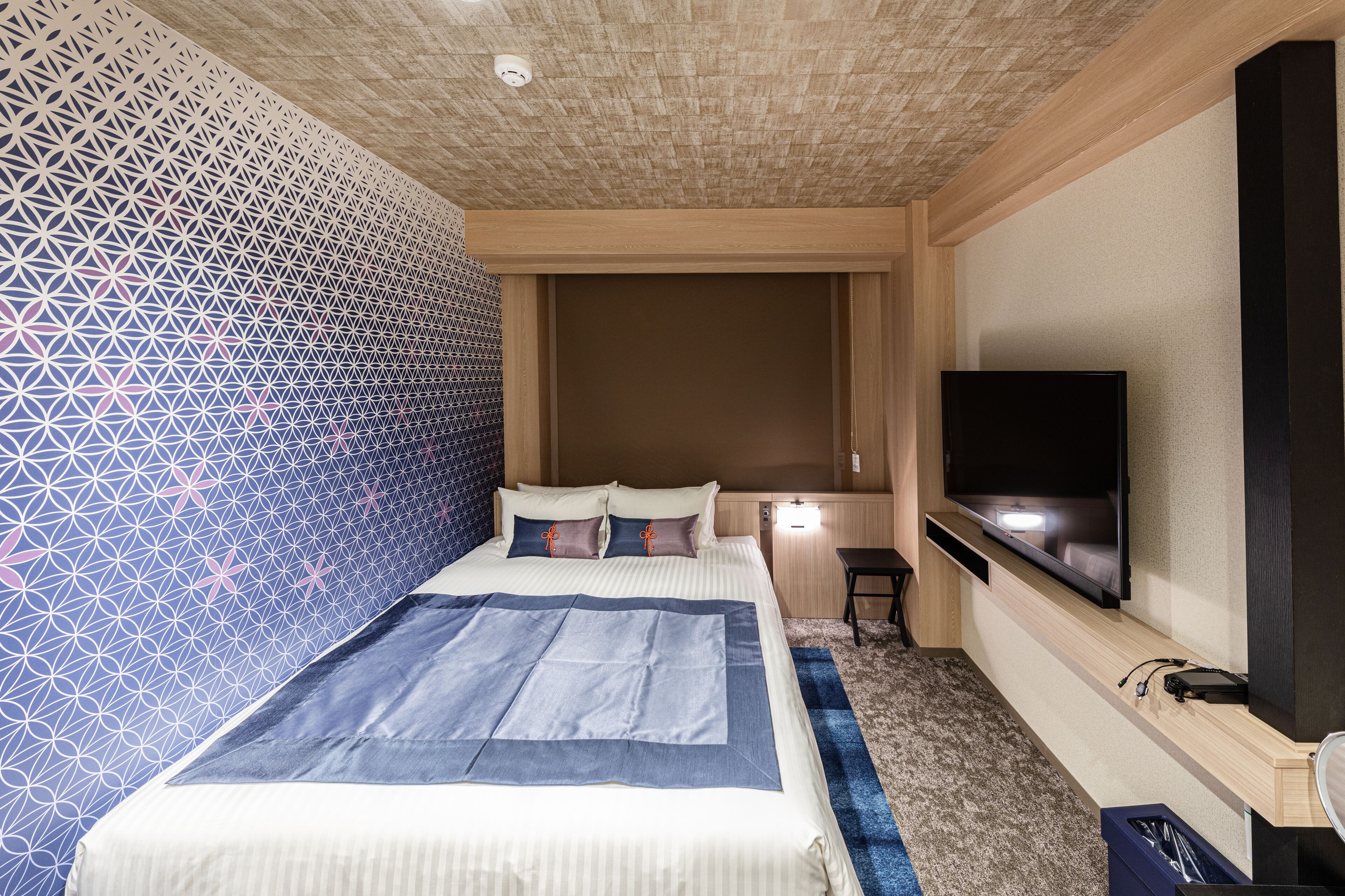 Quarto de hotel com cama, televisão e parede estampada.